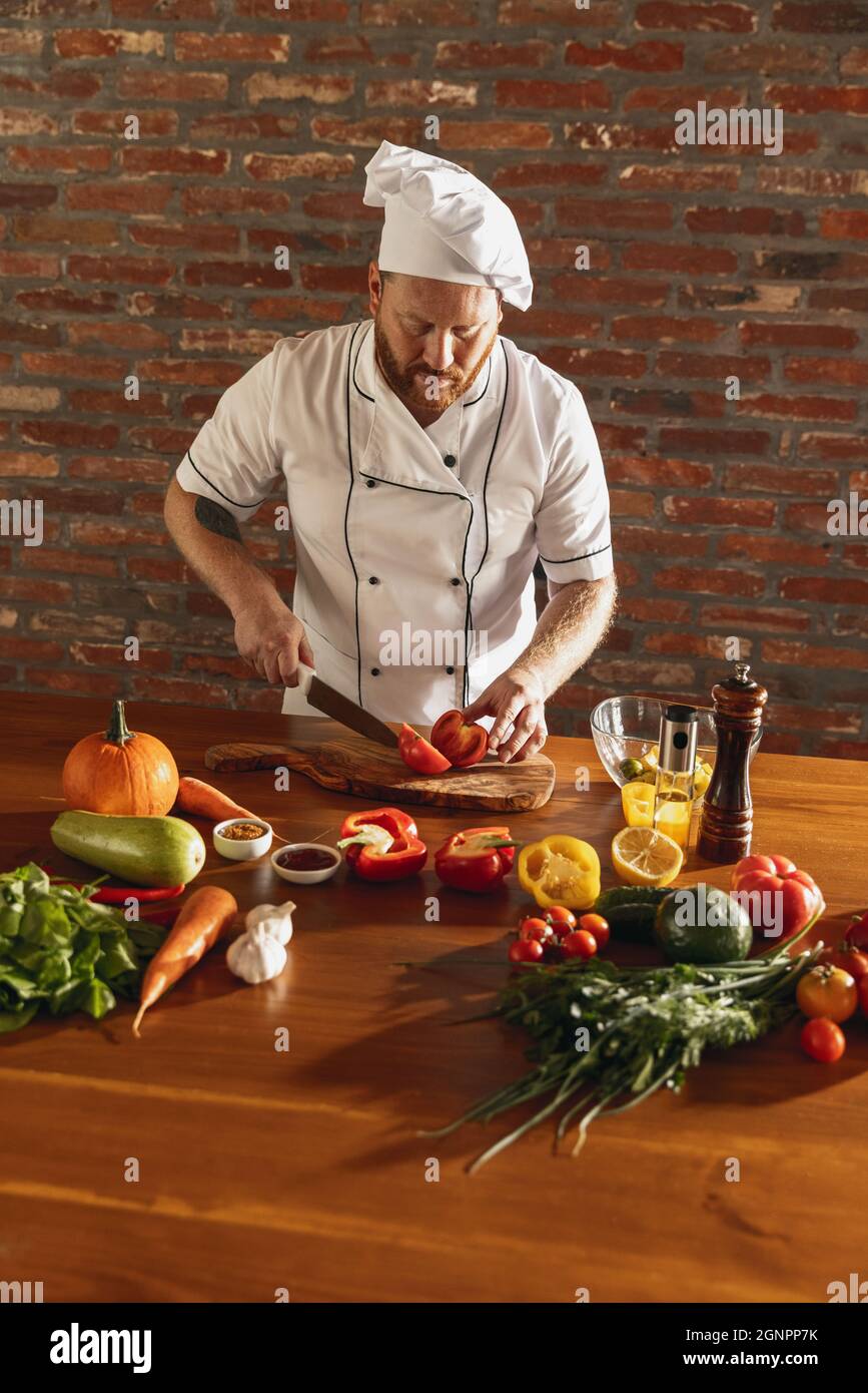 Young Caucasian red-bearded man, chef cooking fresh vegetable salad in ...