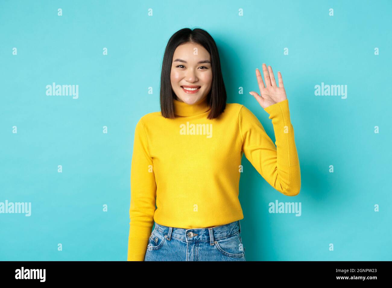 Portrait of beautiful asian girl with happy smile, waving hand to say ...