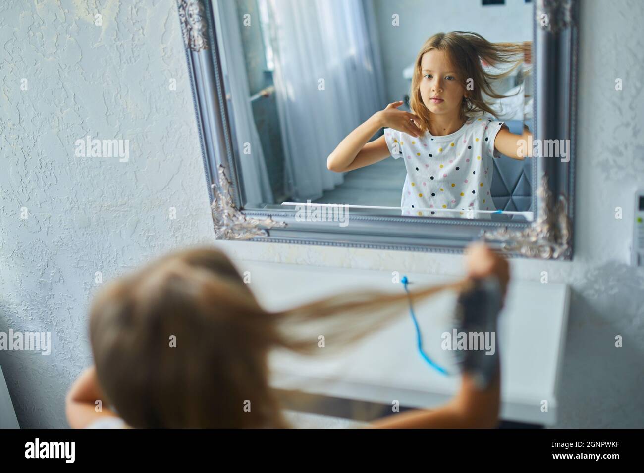 Pretty Little girl combing by herself hair in front of a mirror ...
