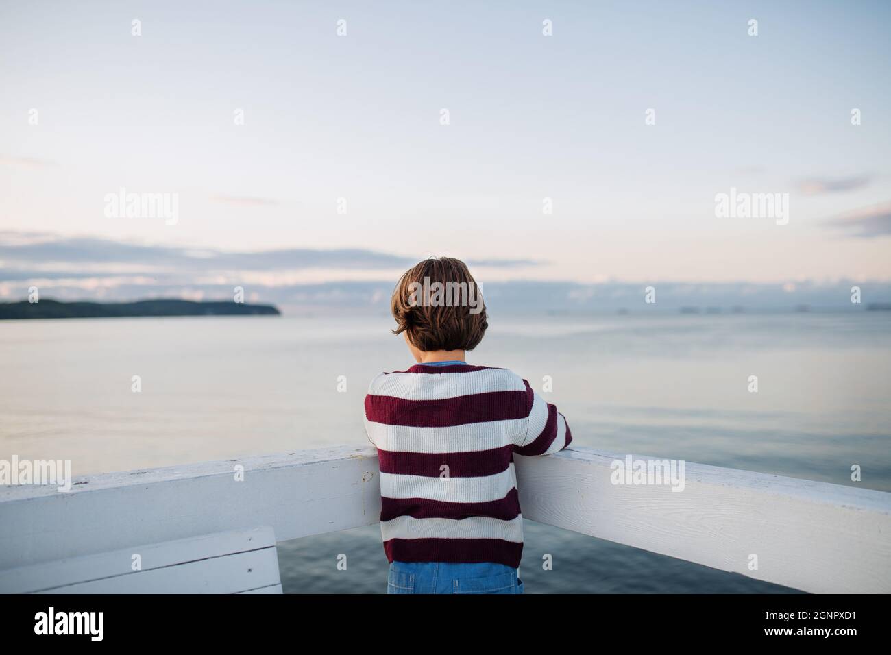 Rear view of preteen girl looking at view outdoors on pier by sea ...