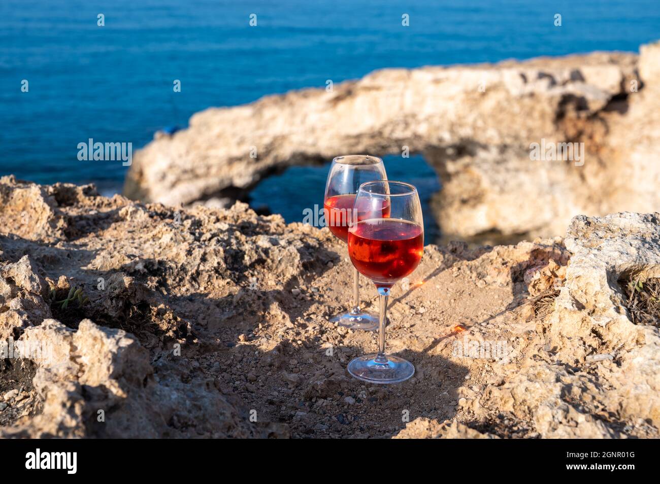 Two glasses of rose dry white wine served on rocks with blue sea bay ...