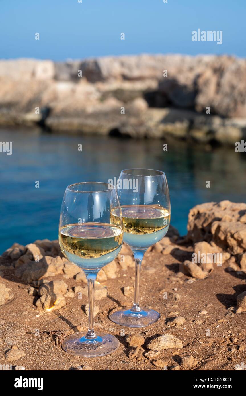 Two glasses of white dry white wine served on yellow rocks in blue sea ...