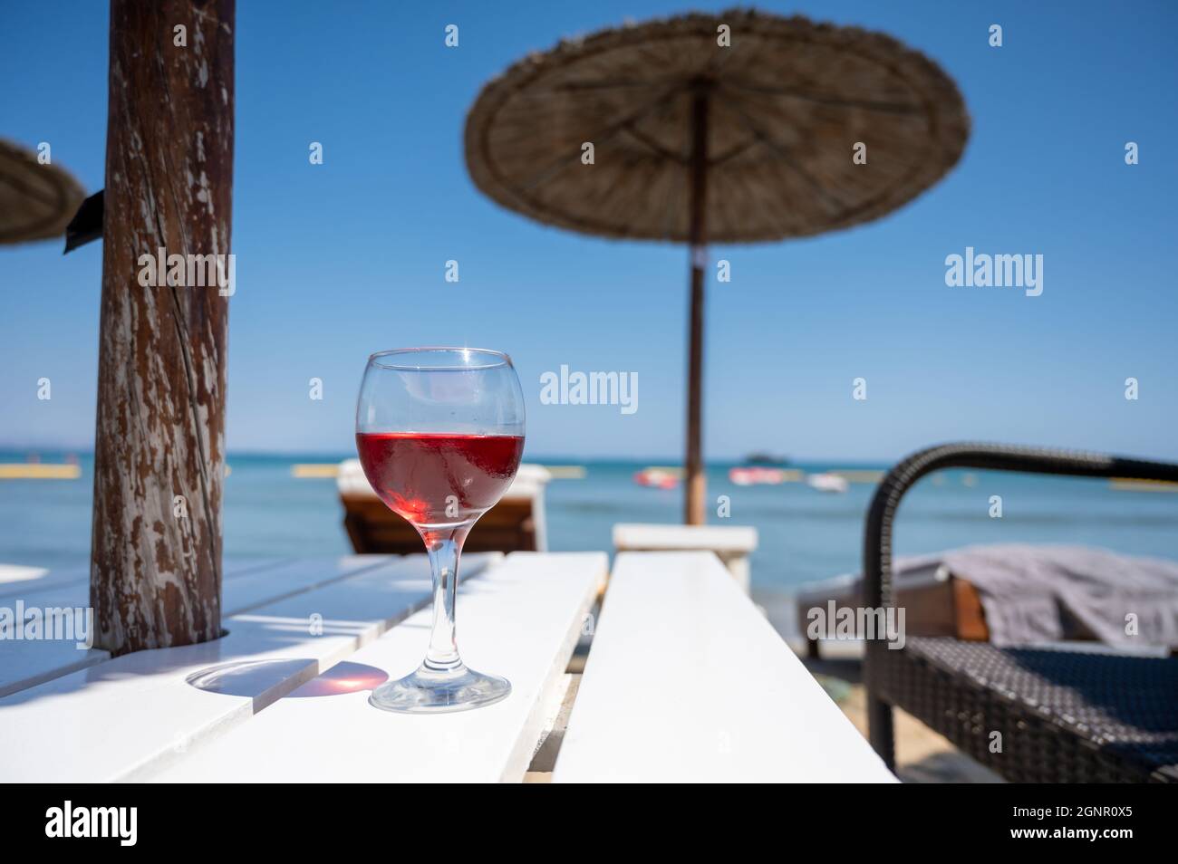 Drinking of cold rose wine in lounge bar on sunny sandy beach with blue ...