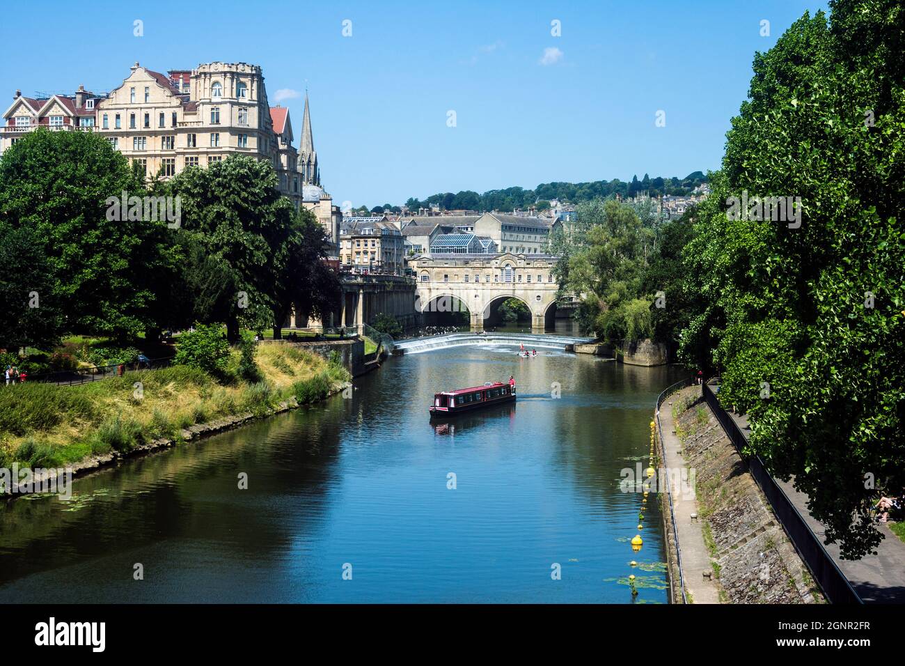 A narrow boat navigates the River Avon with Pulteney Bridge and Weir in ...