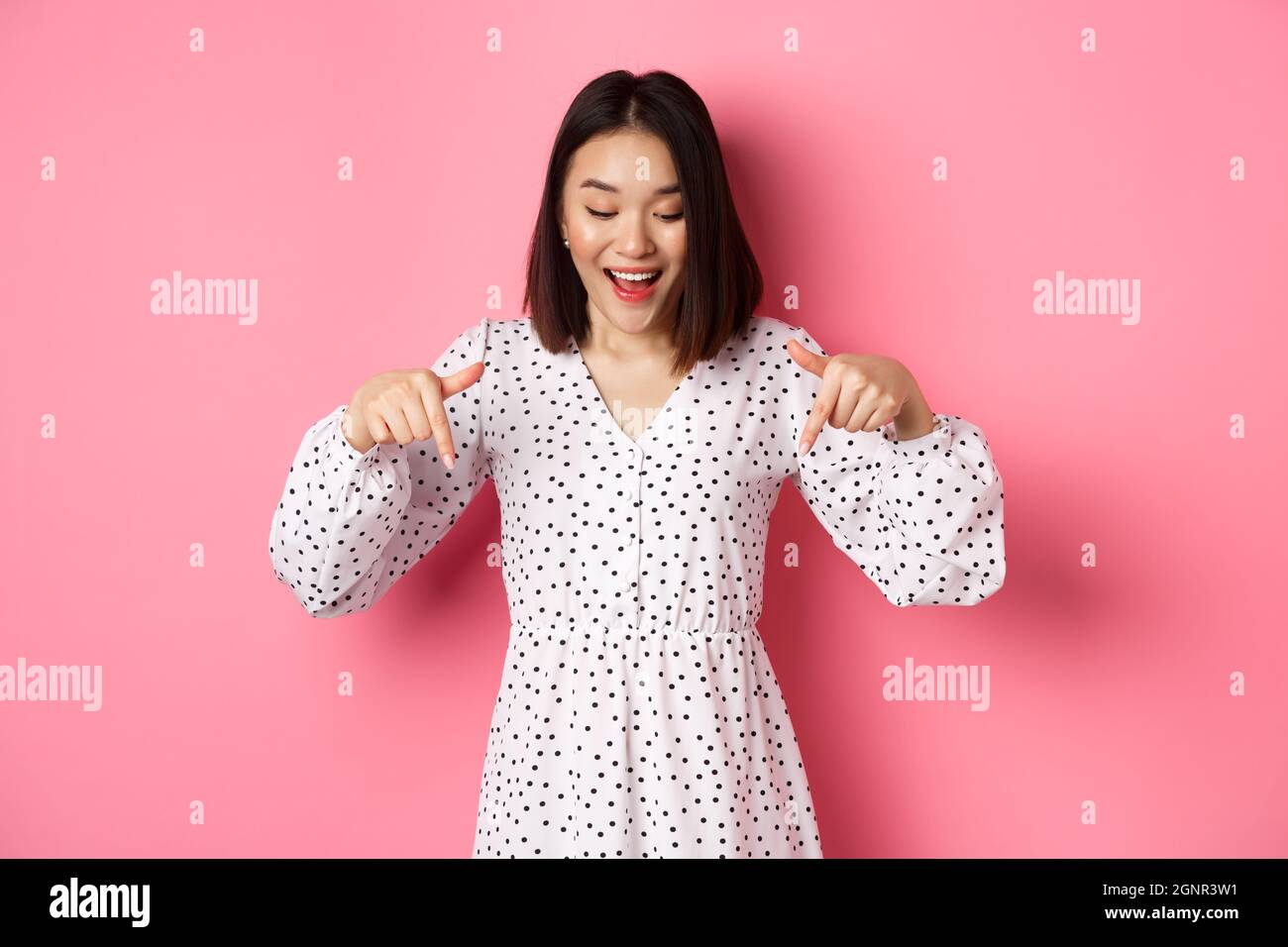 Romantic asian woman peeking down, pointing fingers at bottom, looking ...