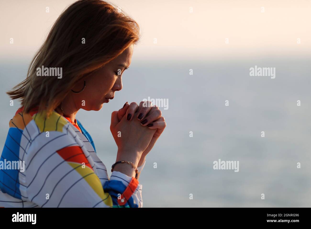 Faithful woman praying, hands folded in worship to god, head down, eyes ...
