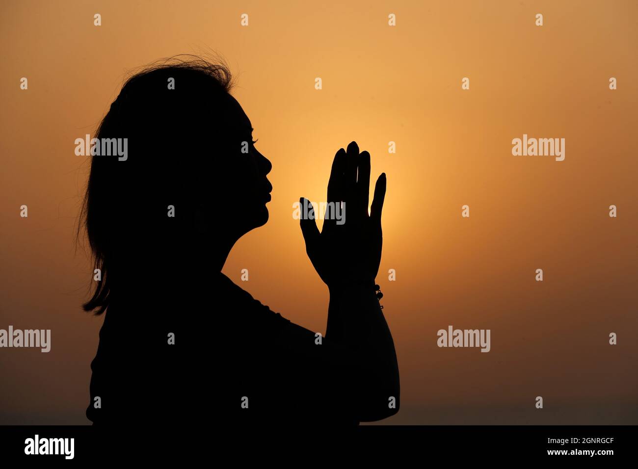 Silhouette at sunset of faithful woman praying. Concept for religion, faith, prayer and ...