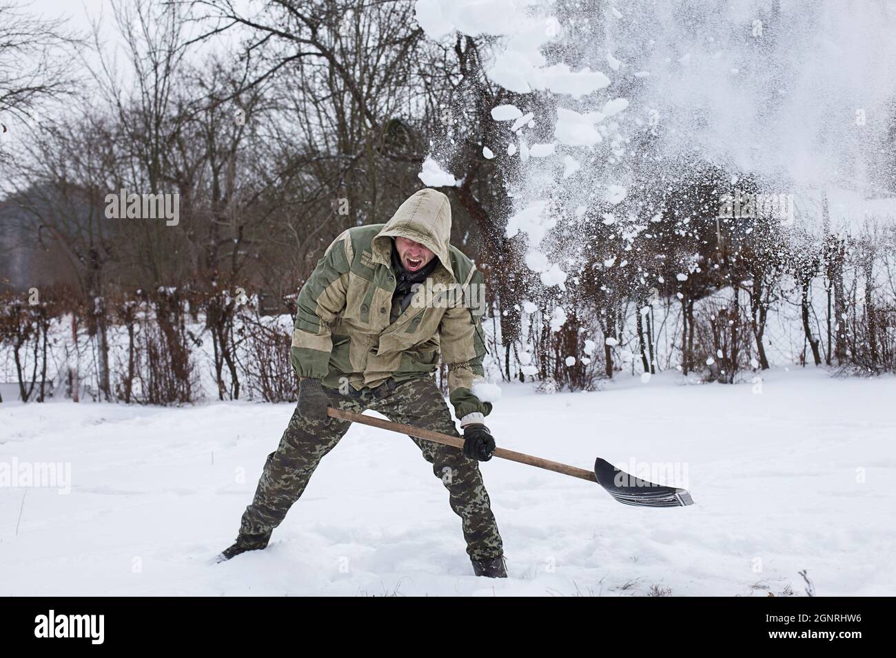 Man in camouflage clears the snow in the yard. Military holding a ...