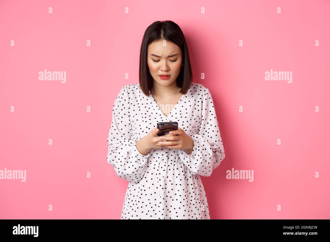 Nervous and concerned asian woman reading message on smartphone ...