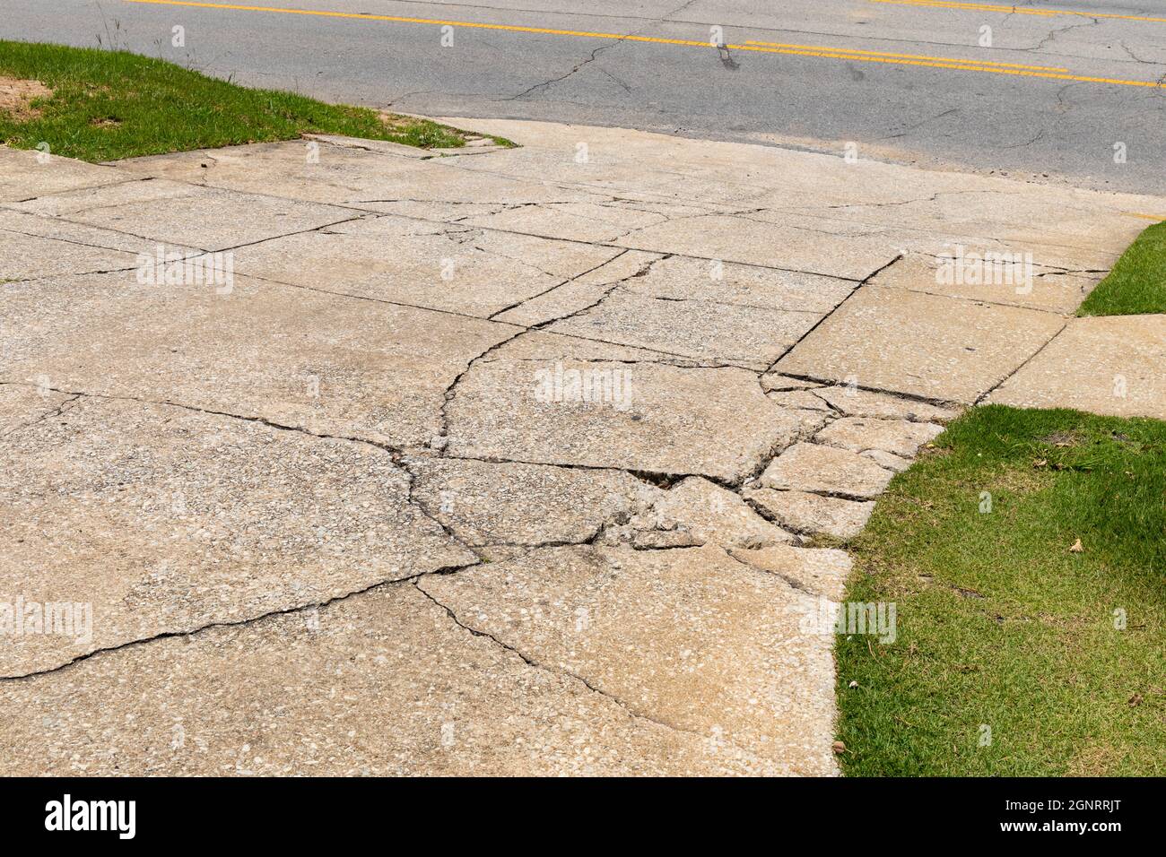 Cracked and broken aggregate concrete driveway descending into an ...