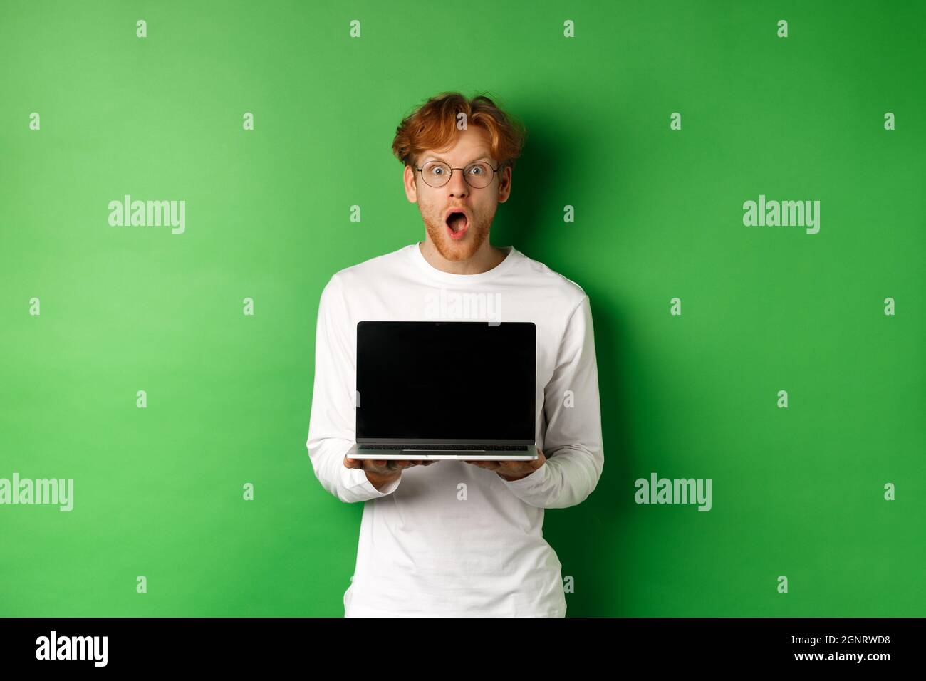 Surprised redhead man in glasses showing laptop blank screen, showing ...