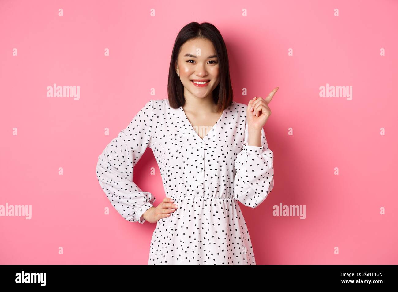 Beautiful asian female model smiling, pointing finger at upper right ...