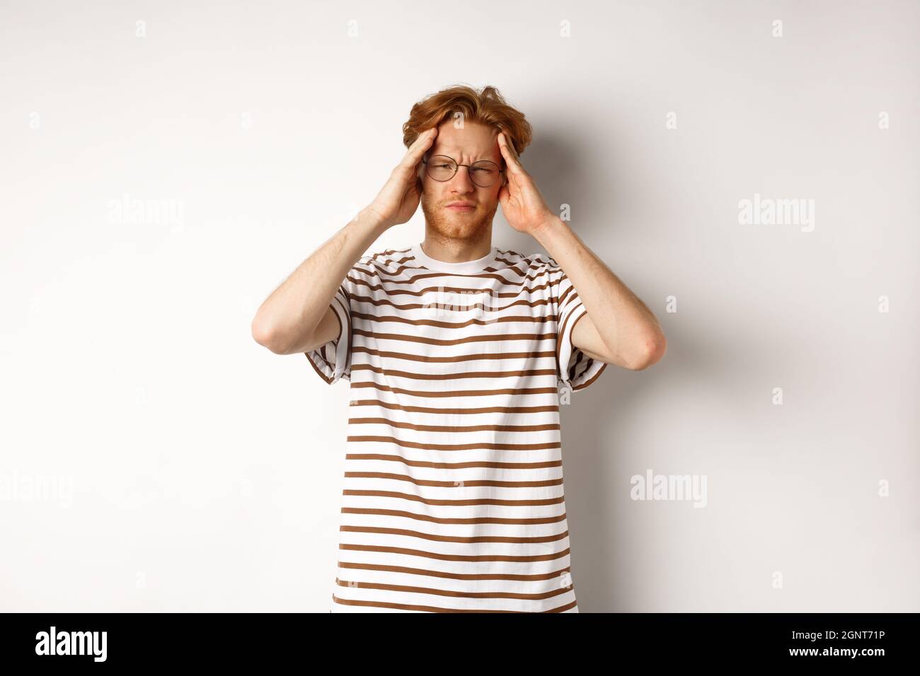 Image of young man with red hair and glasses touching head, frowning ...