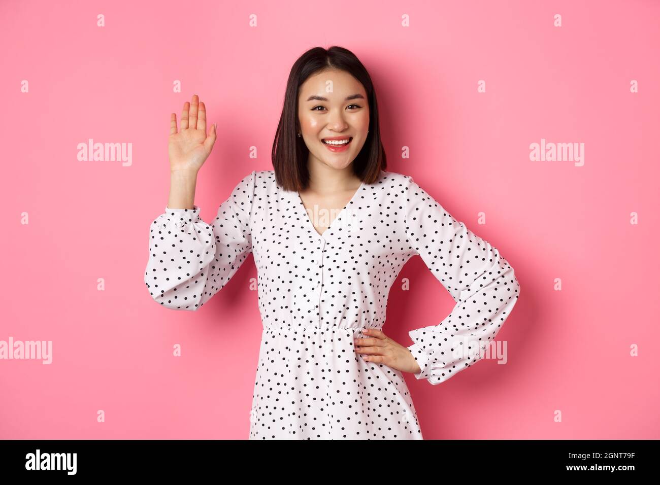 Beautiful asian woman in dress saying hello, waving hand to greet and ...