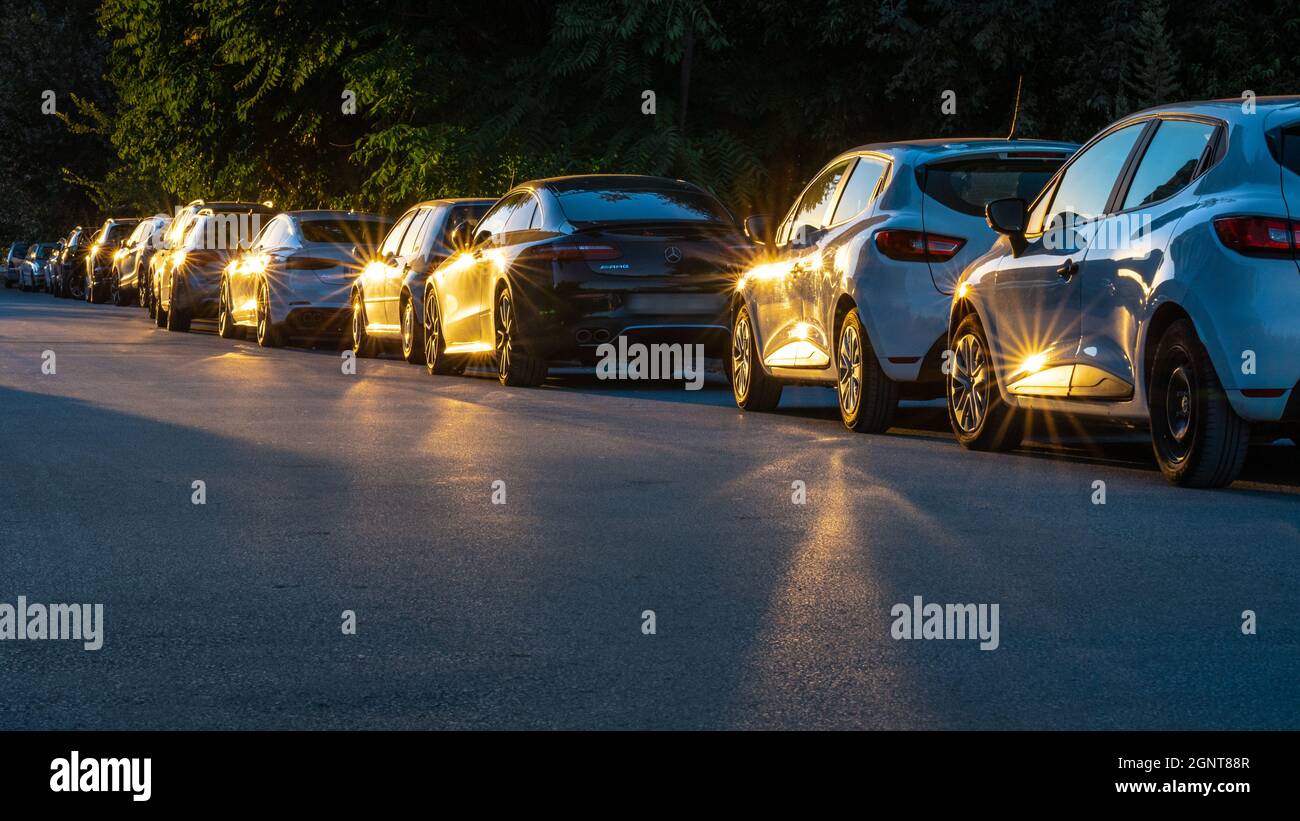 Yellow-orange sun stars during sunset on a long line of parked cars in ...