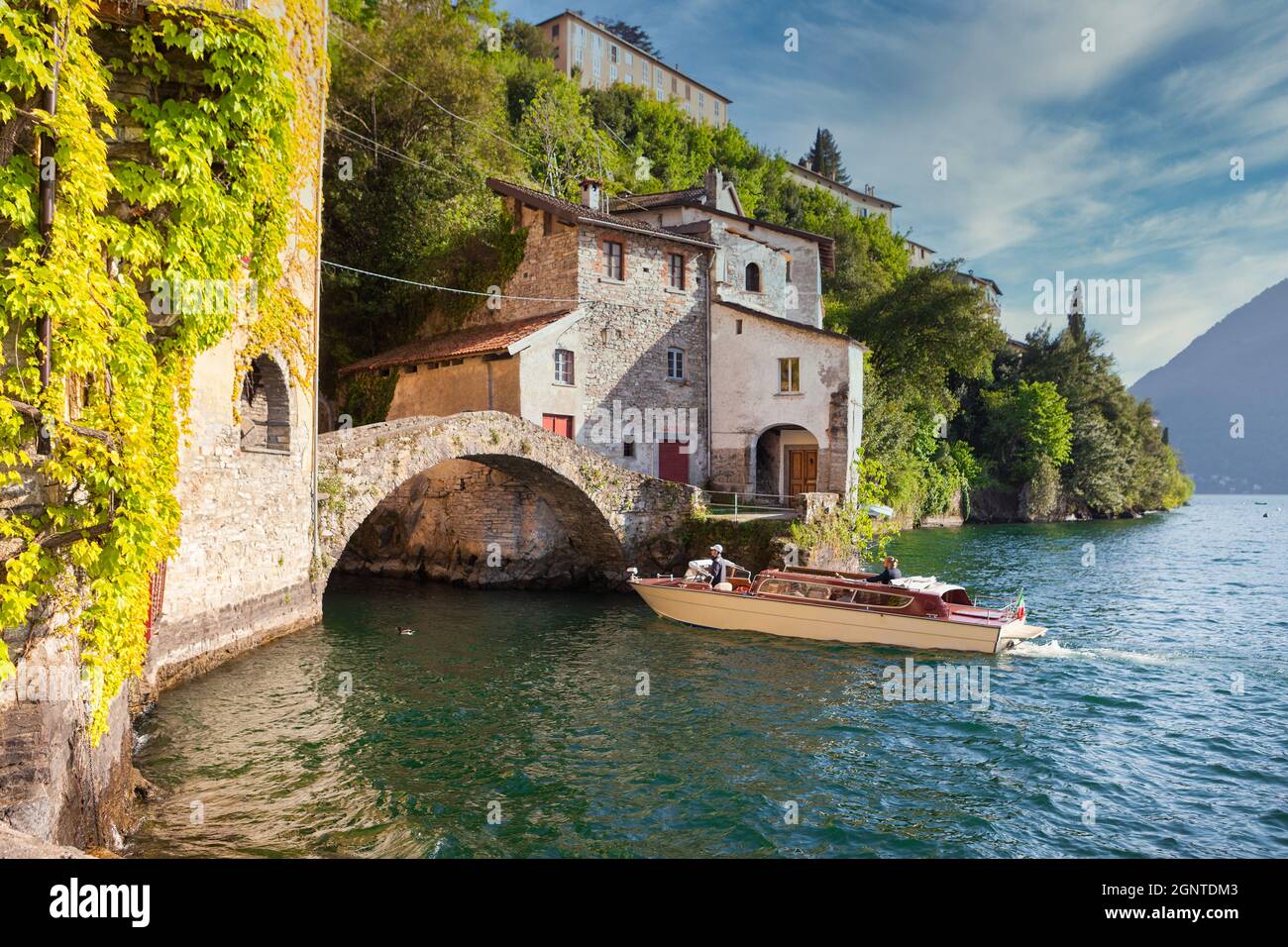 Fashioned touristic wooden speedboat approaching an old stone bridge at ...