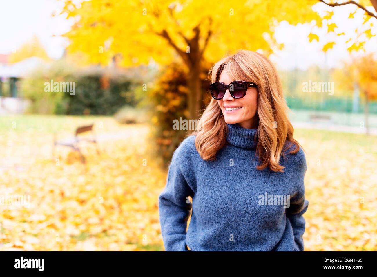 Happy middle aged woman wearing sunglasses and sweater while standing ...