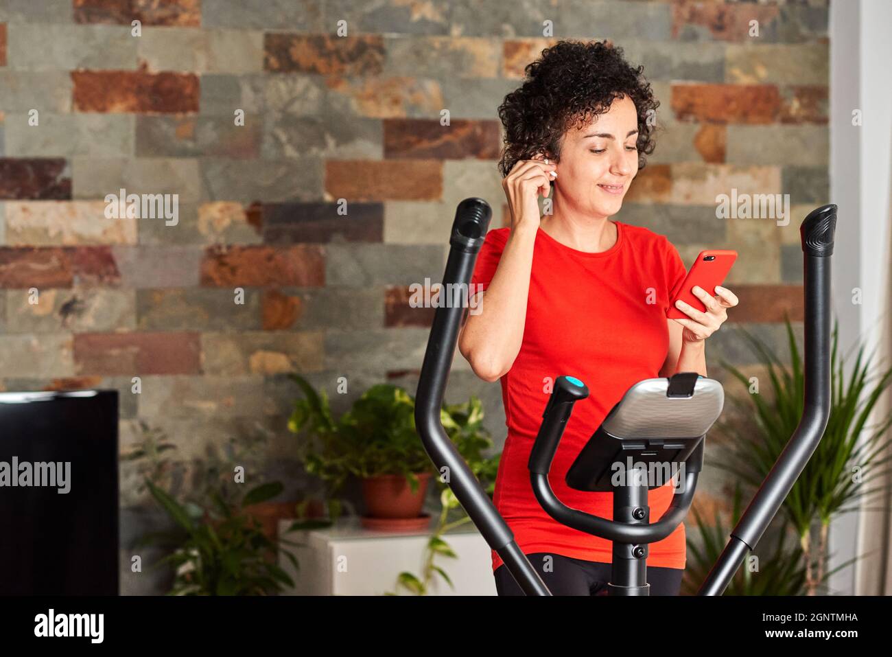 Woman exercising at home on cross training elliptical using mobile ...