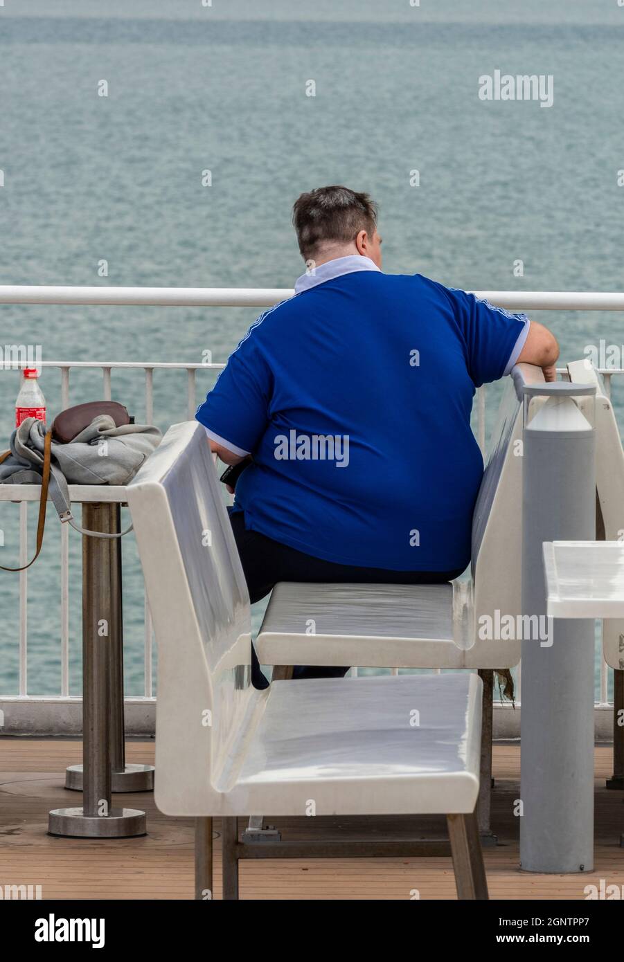 Overweight or obese man sitting on plastic bench or seating at the ...