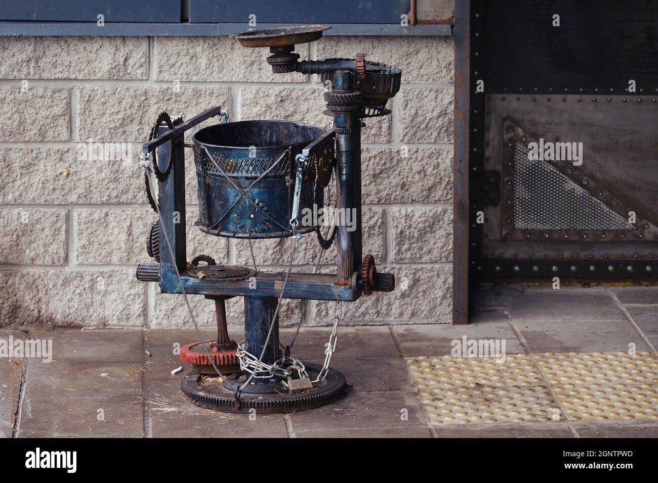 An unusual steampunk style trash can with mechanisms, gears and chains ...