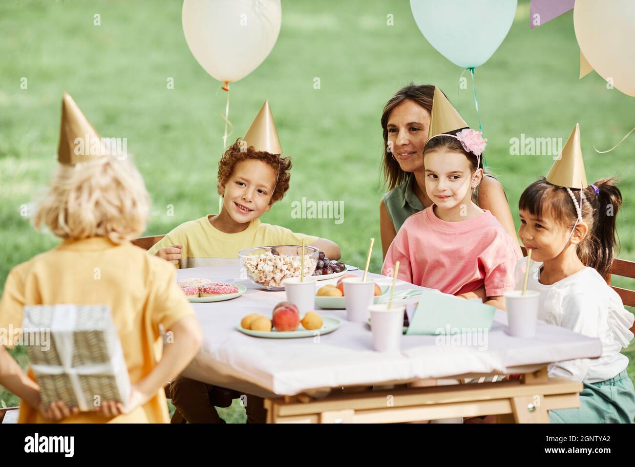 Back view at little boy hiding gift during outdoor Birthday party in ...