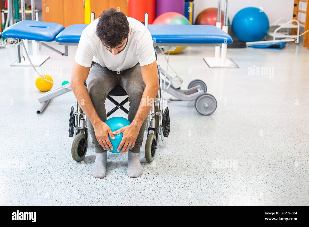 Disabled man seated in a wheelchair, doing an exercise with a smaller ...