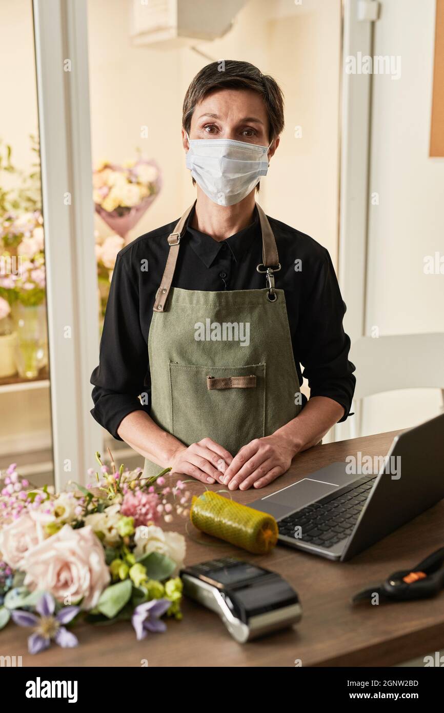 Vertical portrait of female shop assistant wearing mask while standing ...