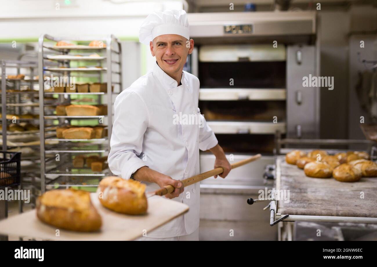 Baker taking out from oven baked bread Stock Photo - Alamy