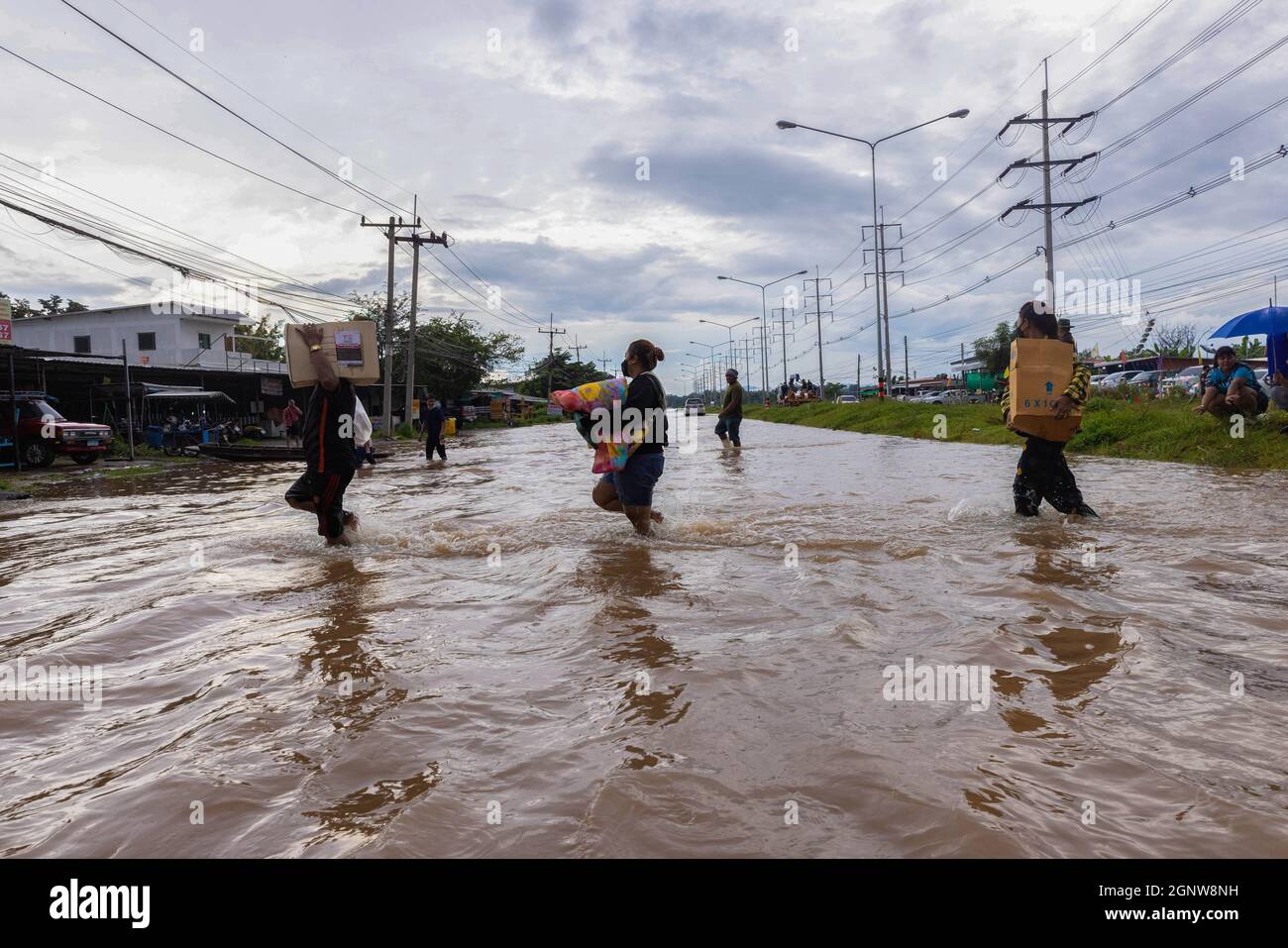 People walk through a submerged road after a heavy rainfall. Lopburi ...