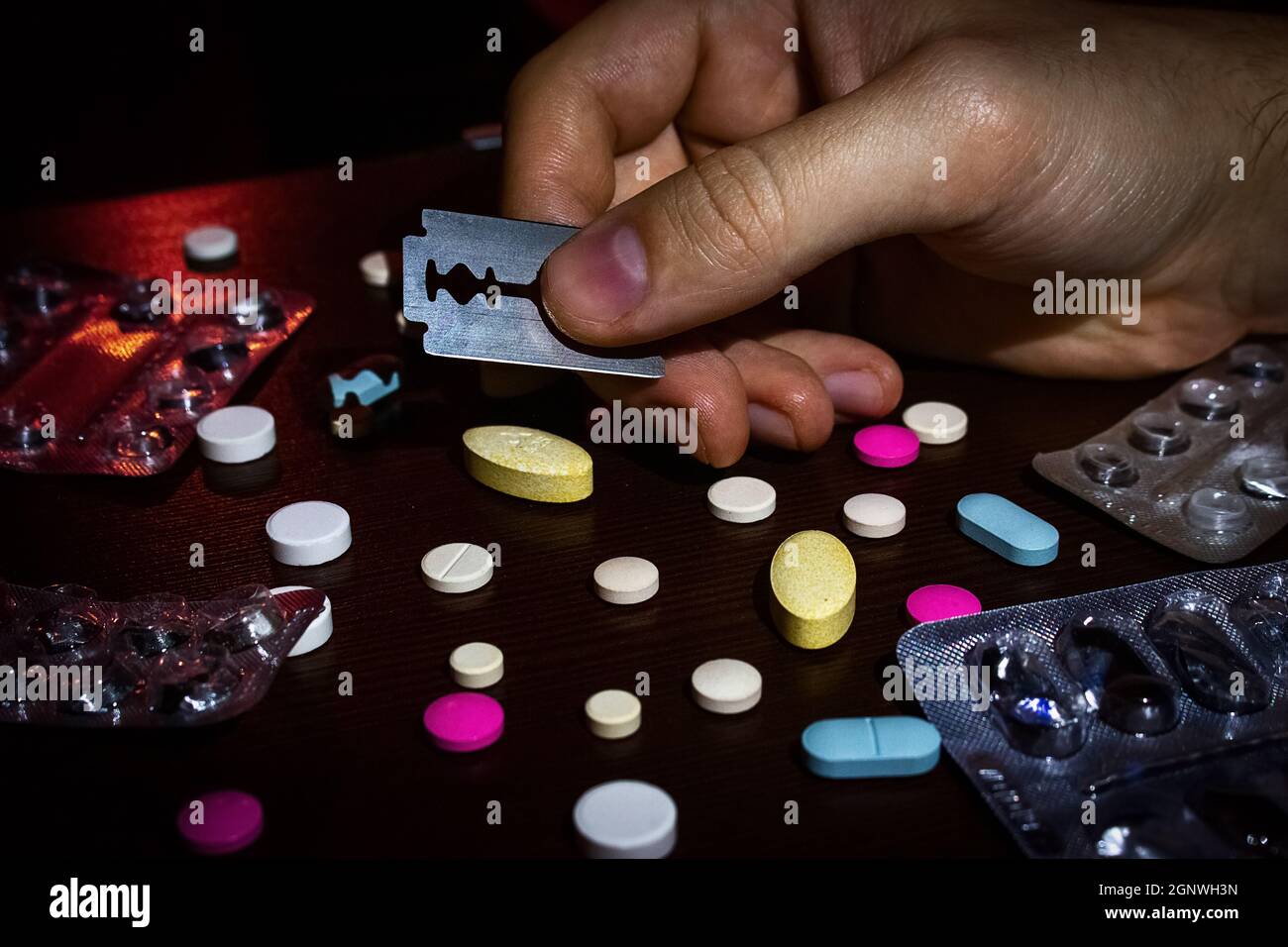 holding a blade in his hand on the background of pills drugs concept ...