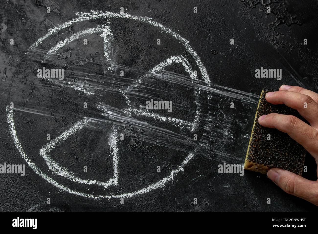 hand with a sponge erases the symbol of nuclear weapons on a black ...