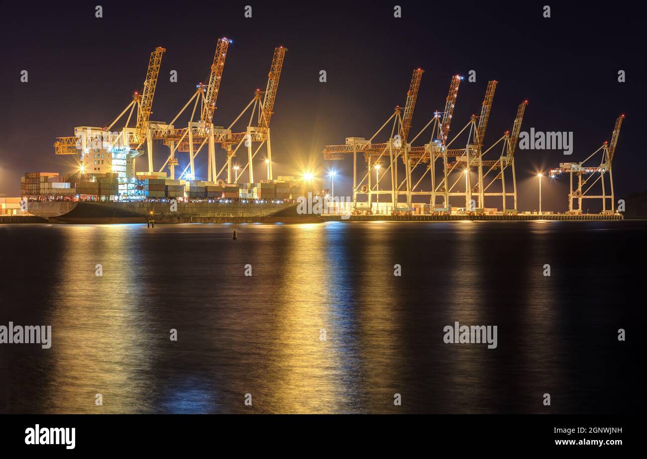 A port at night. A container vessel is at the wharf below a row of ...