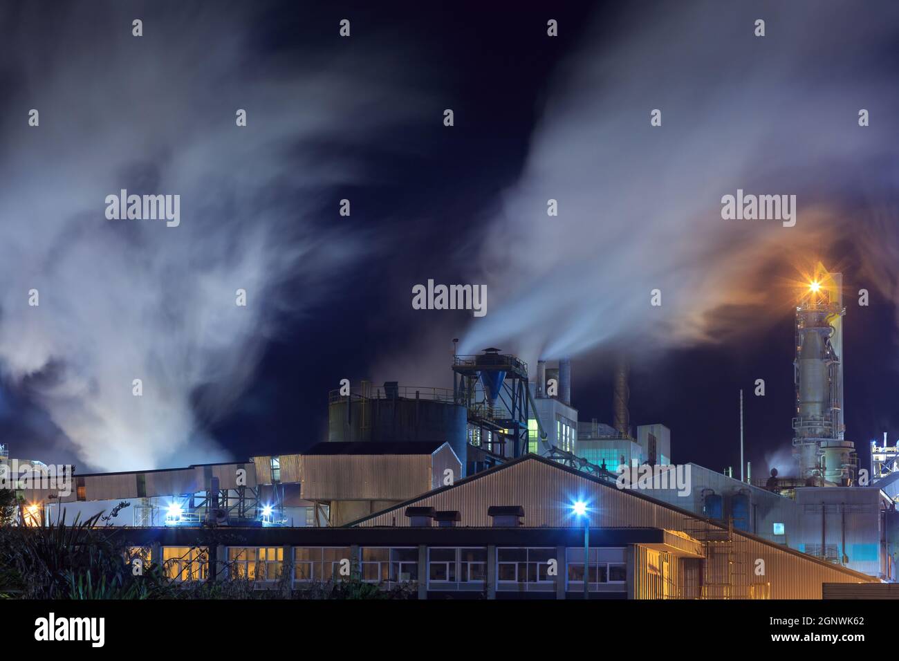 A pulp and paper mill at nighttime, with steam billowing from the ...