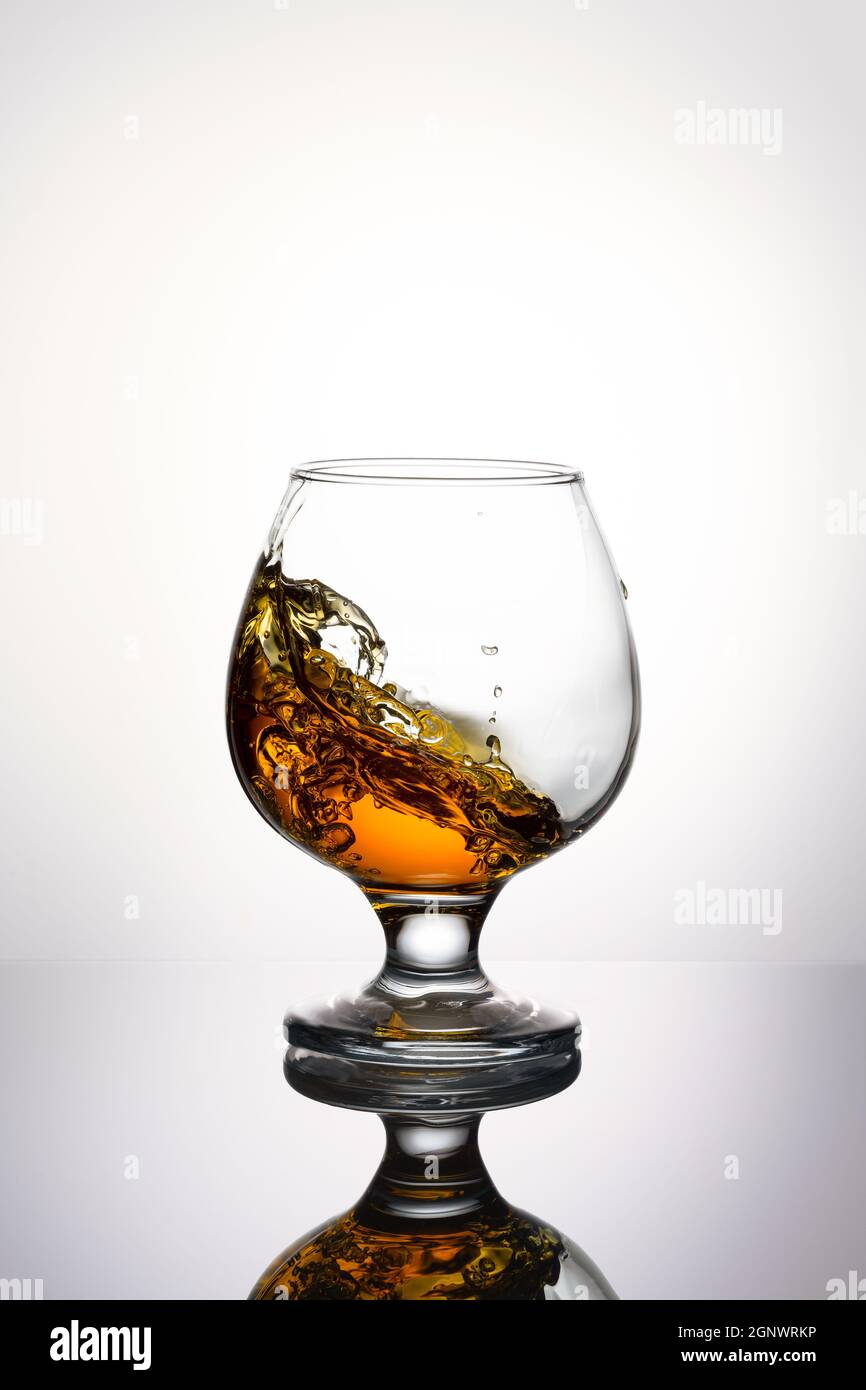 Splash of cognac in glass isolated on a light background Stock Photo ...