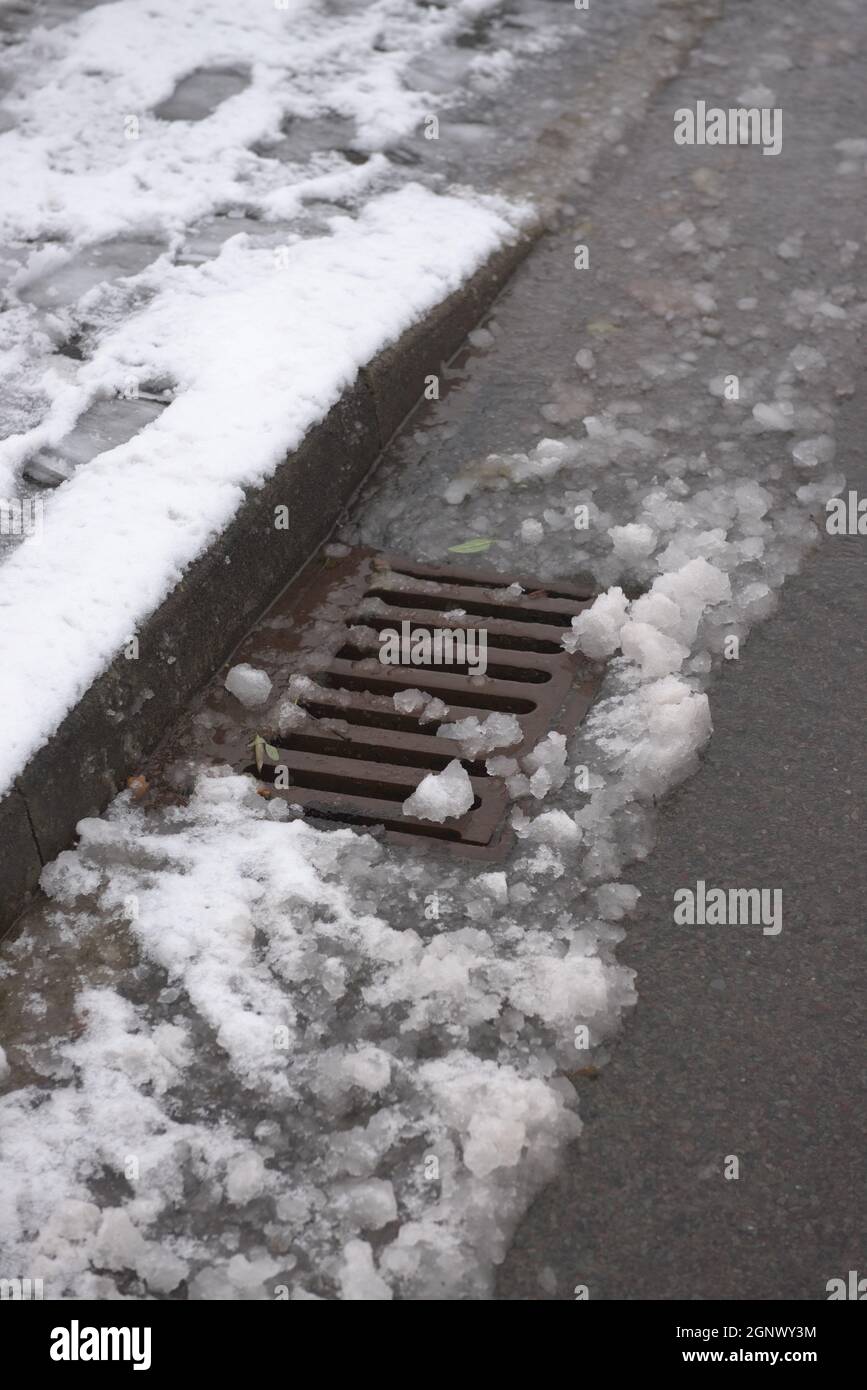 7 - Urban highway drain covered in thawing snow fall. Water runs along ...