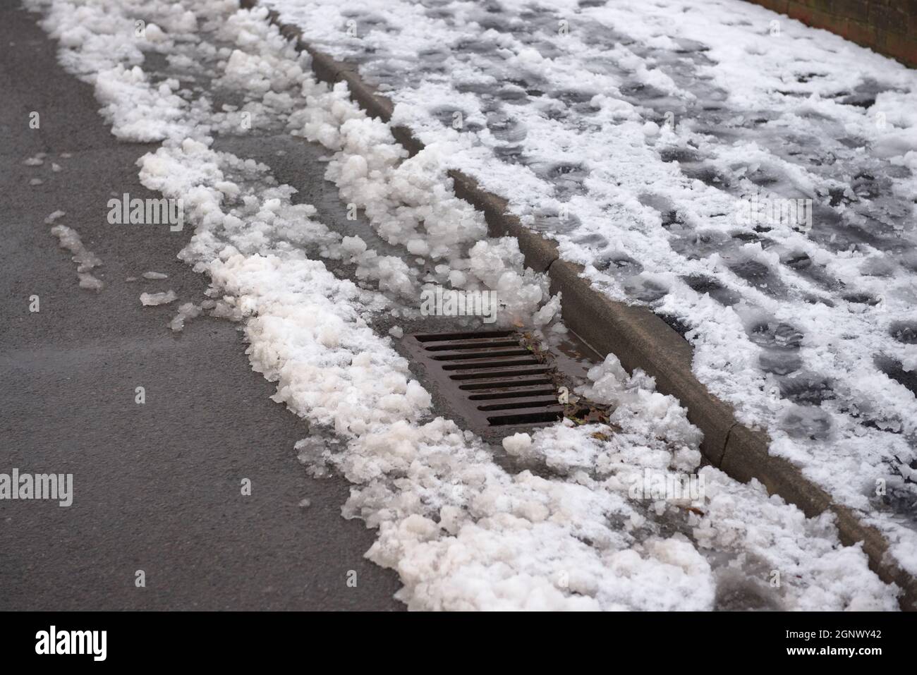12 - Urban scene of footsteps in a pavement full of snow. Drain emerges ...
