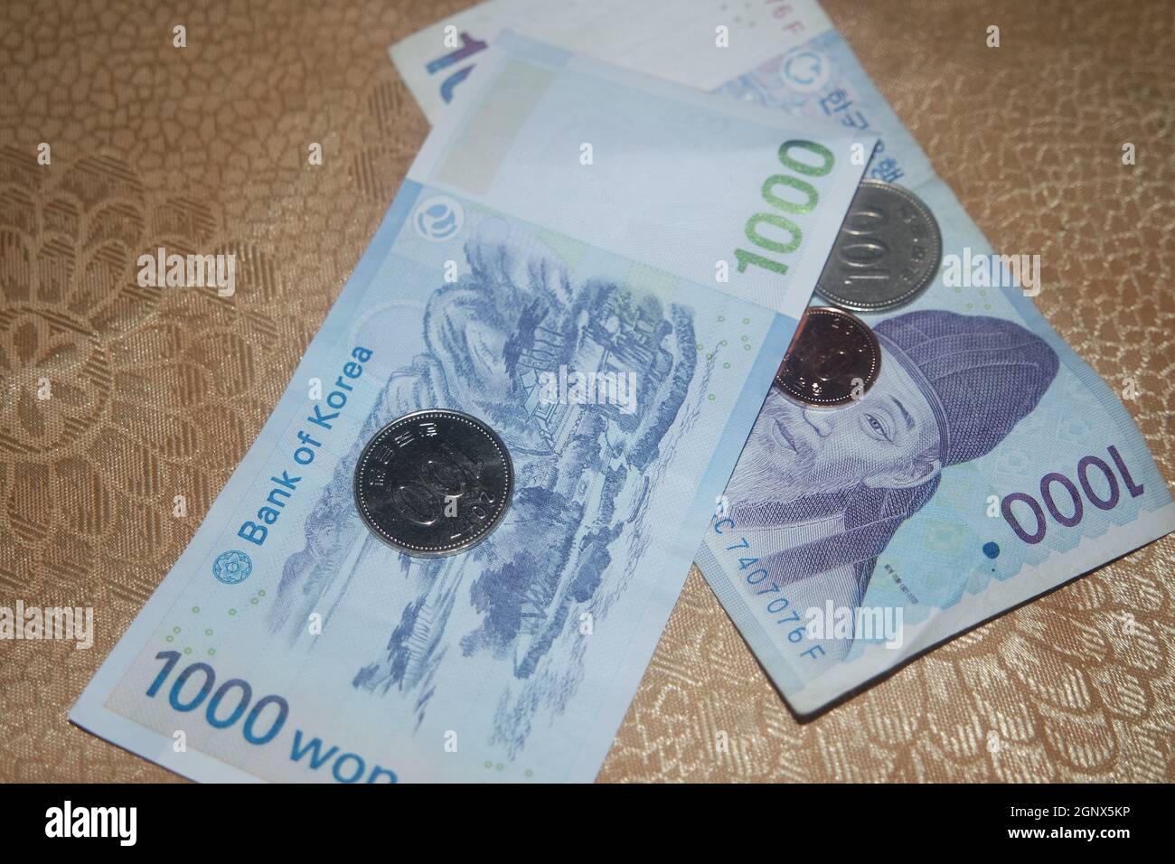 Silver shining Korean won coin scattered over Korean notes on a wooden ...