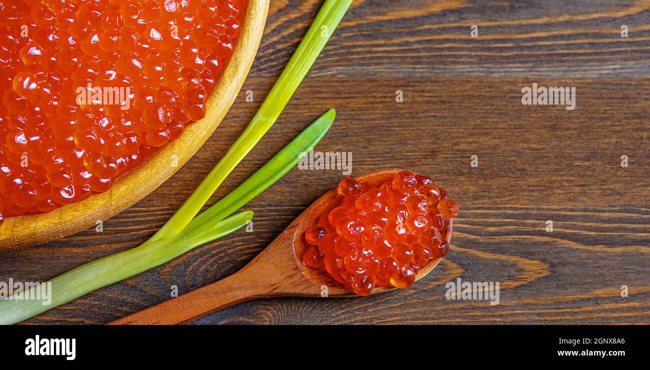 Red caviar in a wooden cup on a wooden background with a spoon. Place ...