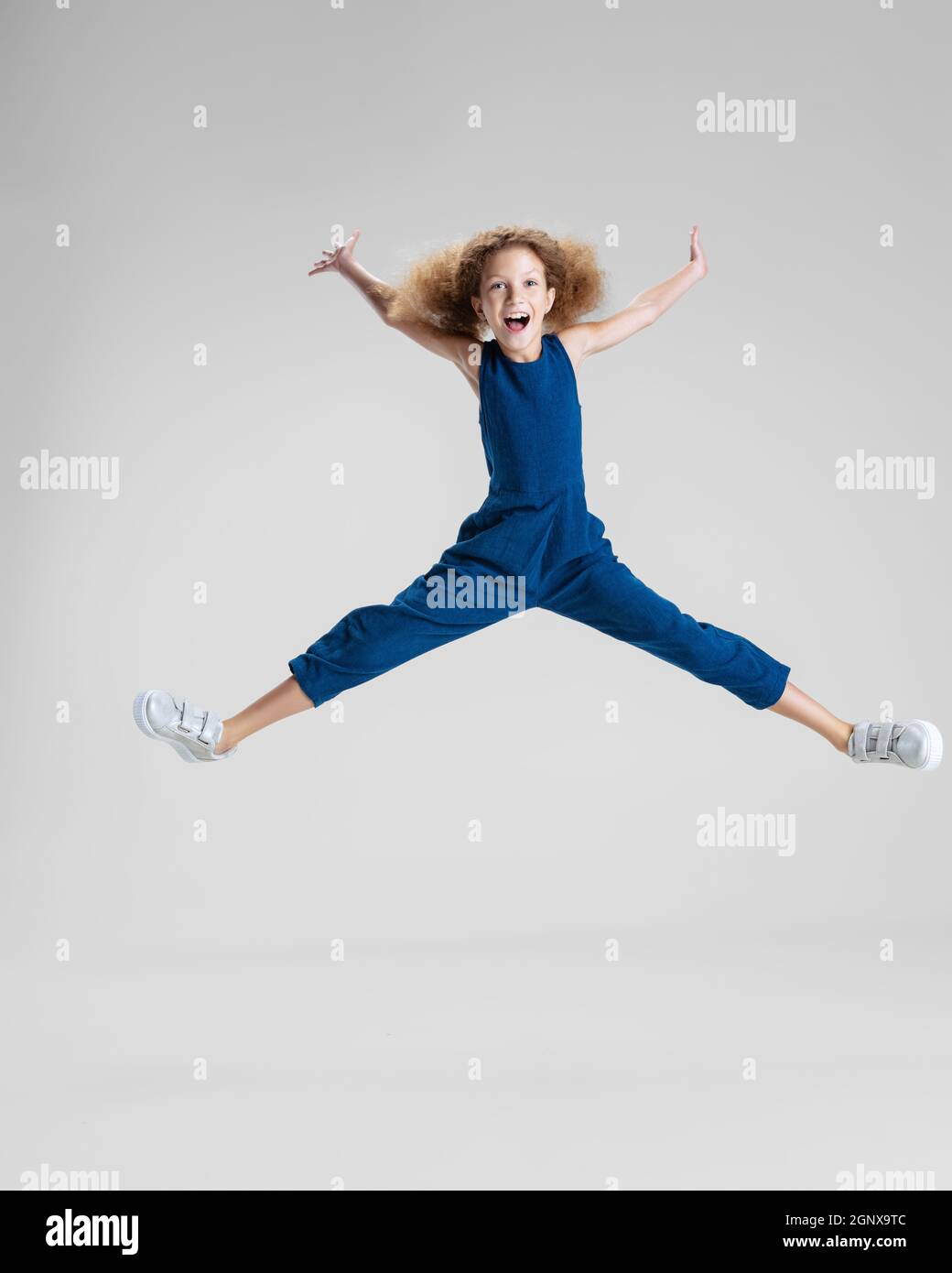 One little Caucasian cute girl in blue stylish jumpsuit jumping high ...