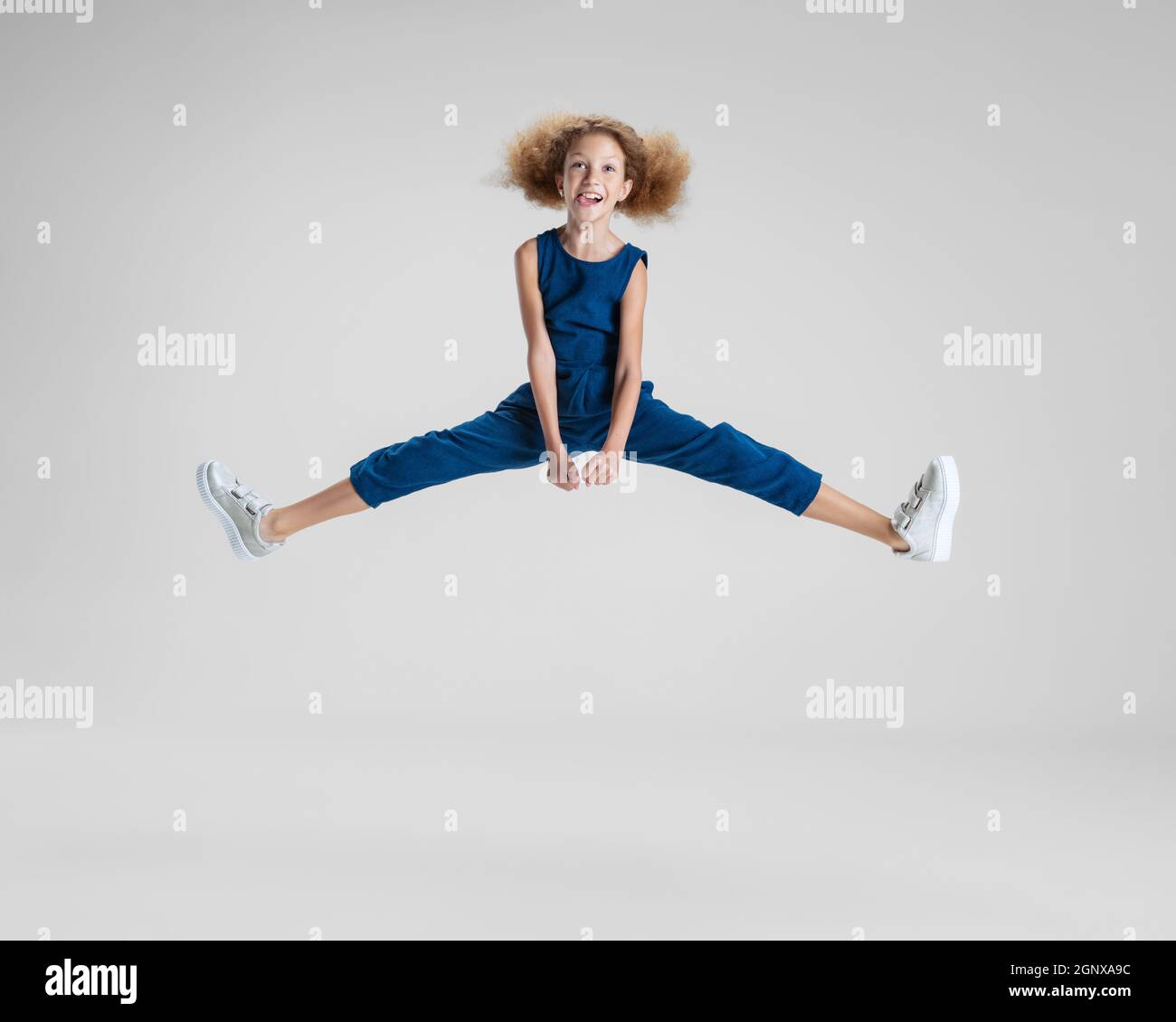 One little Caucasian cute girl in blue stylish jumpsuit jumping high ...