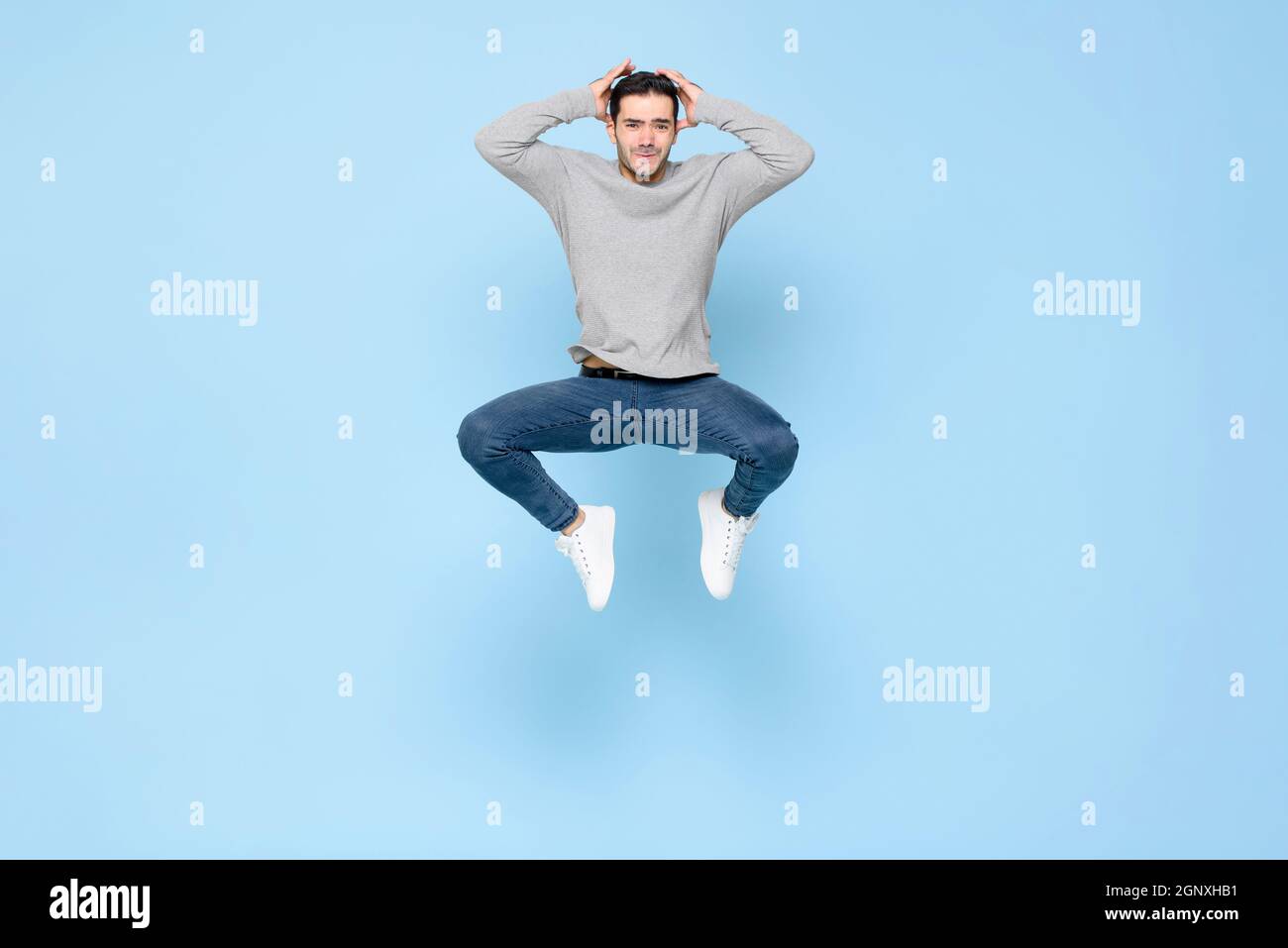 Young handsome man feeling overwhelmed jumping with hands on head in ...