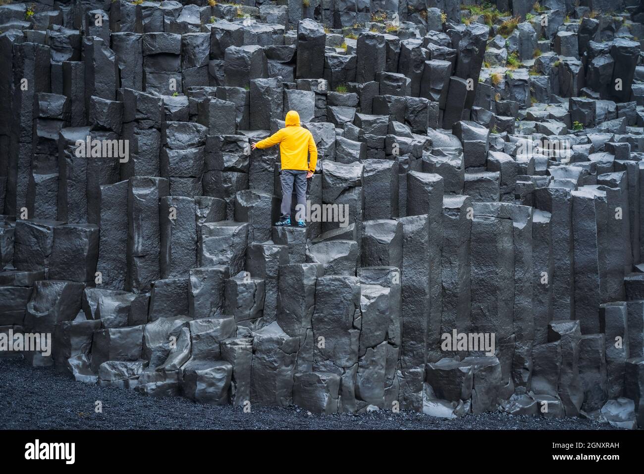 Man wearing yellow coat looking up at Reynisdrangar basalt columns at ...