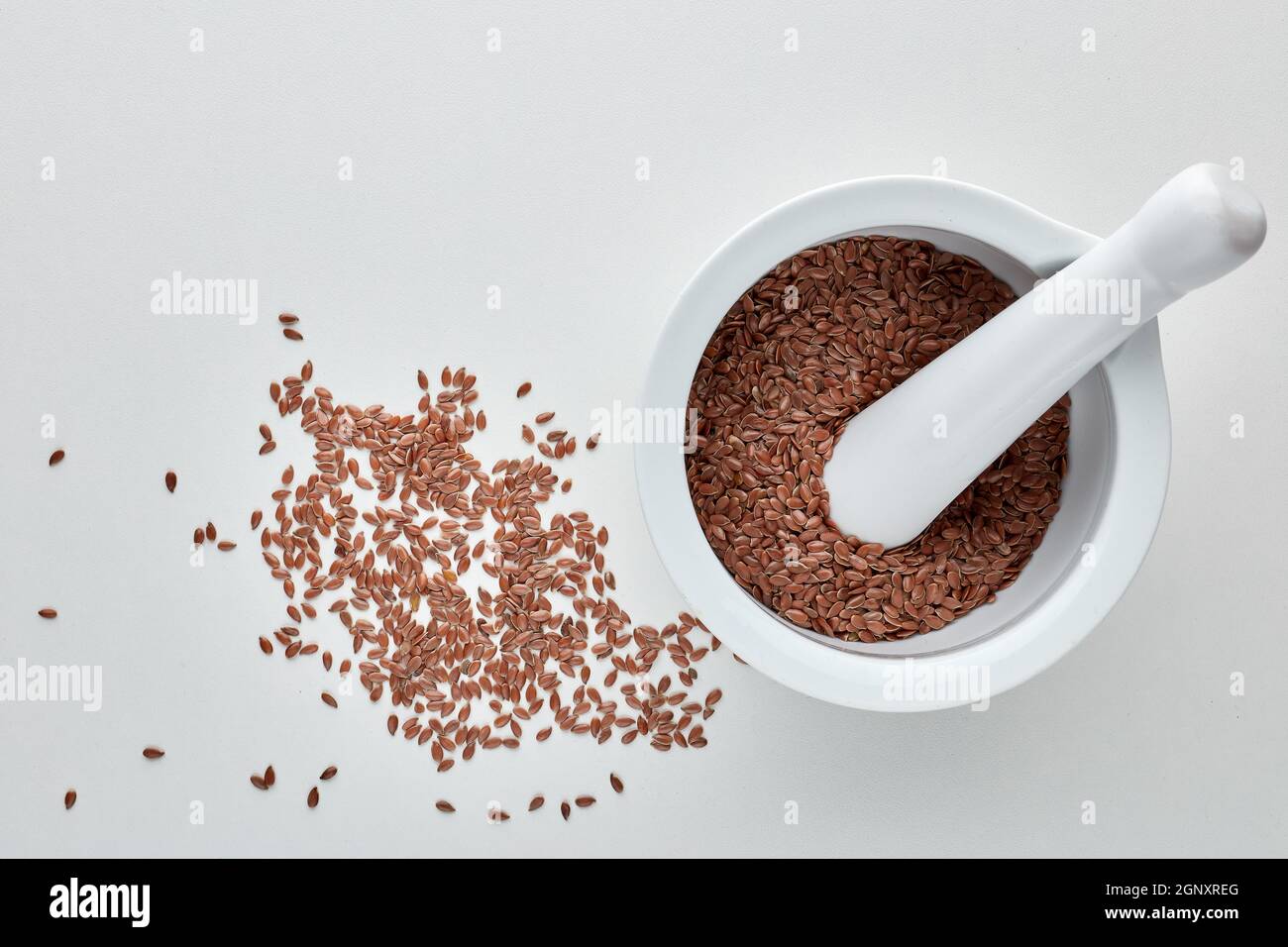Flax seeds in porcelain mortar with pestle on white background. Top view with copy space ...