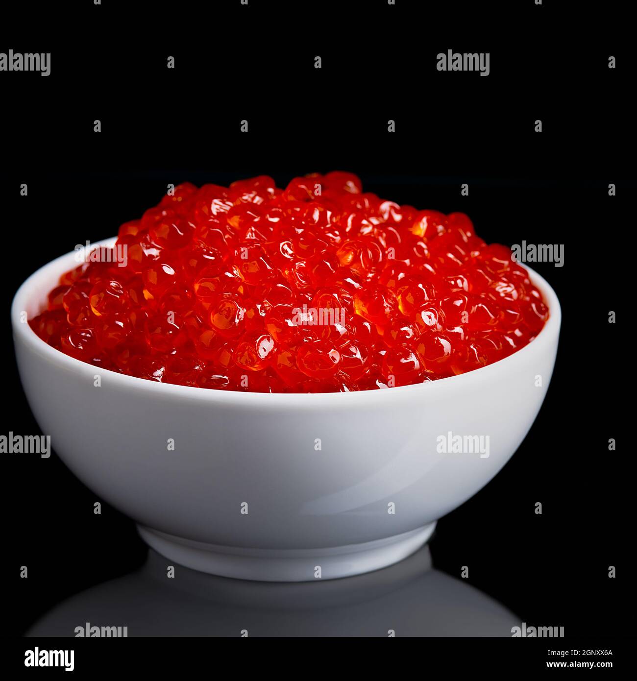 Red caviar in a white cup on a black background with a reflection ...