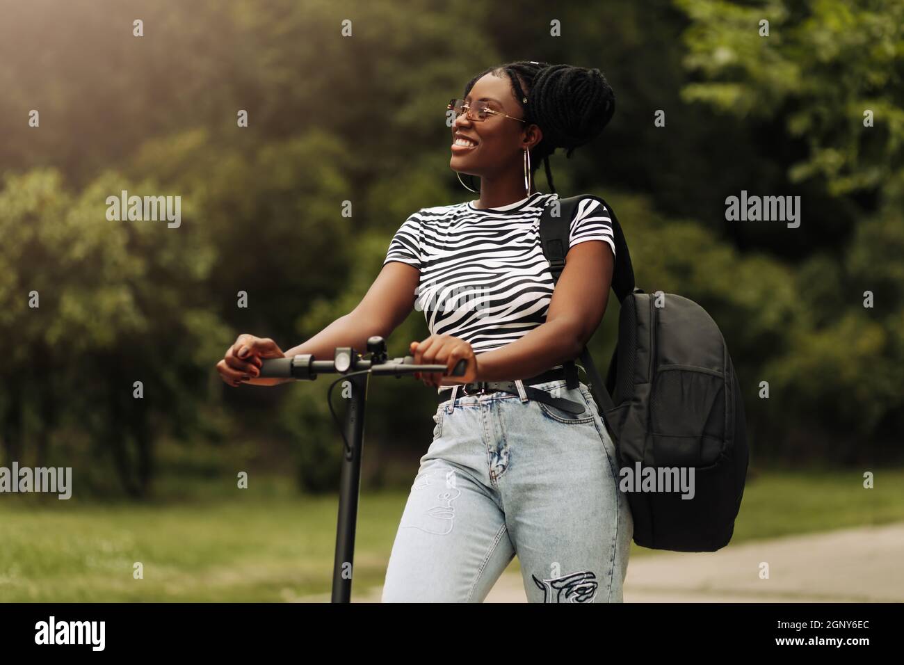 Happy black female student, with a backpack, rides an electric scooter ...