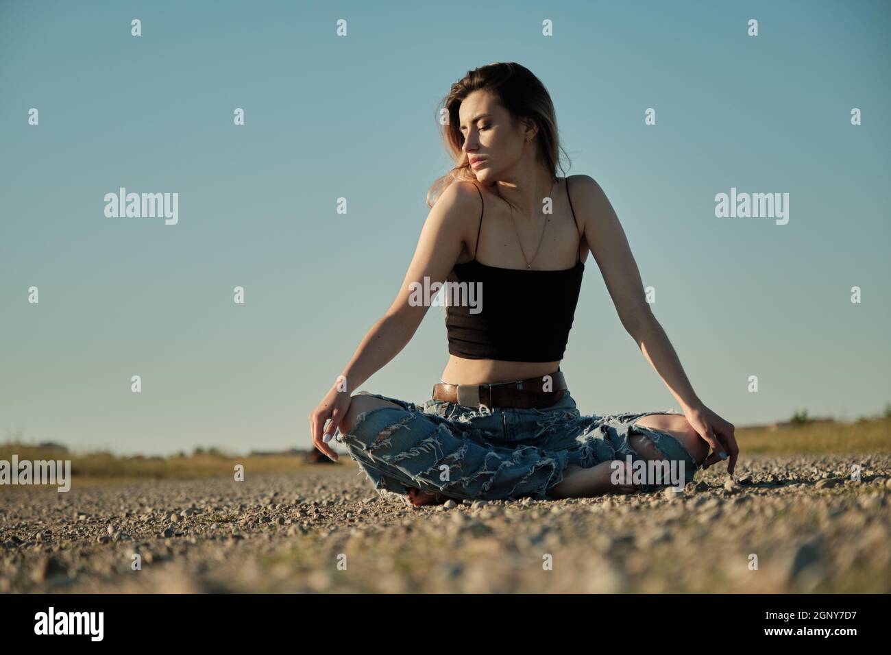 serious sad tramp girl in torn jeans sits on a deserted road Stock ...