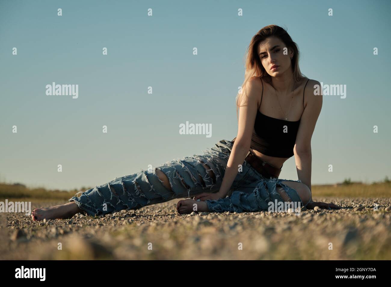 serious sad tramp girl in torn jeans sits on a deserted road Stock ...