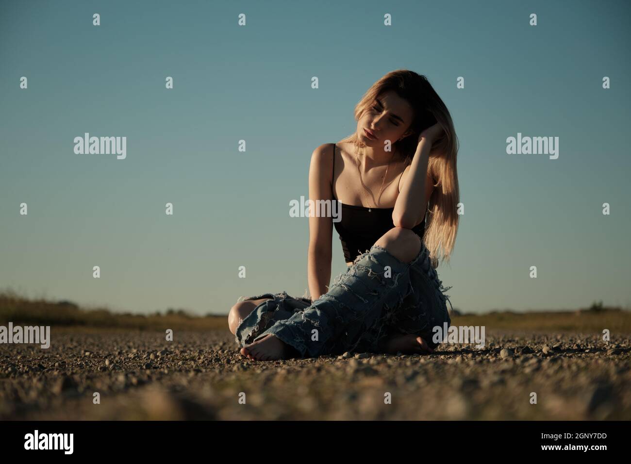 serious sad tramp girl in torn jeans sits on a deserted road Stock ...