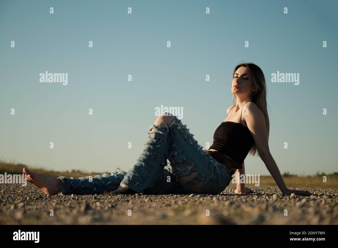 serious sad tramp girl in torn jeans sits on a deserted road Stock ...