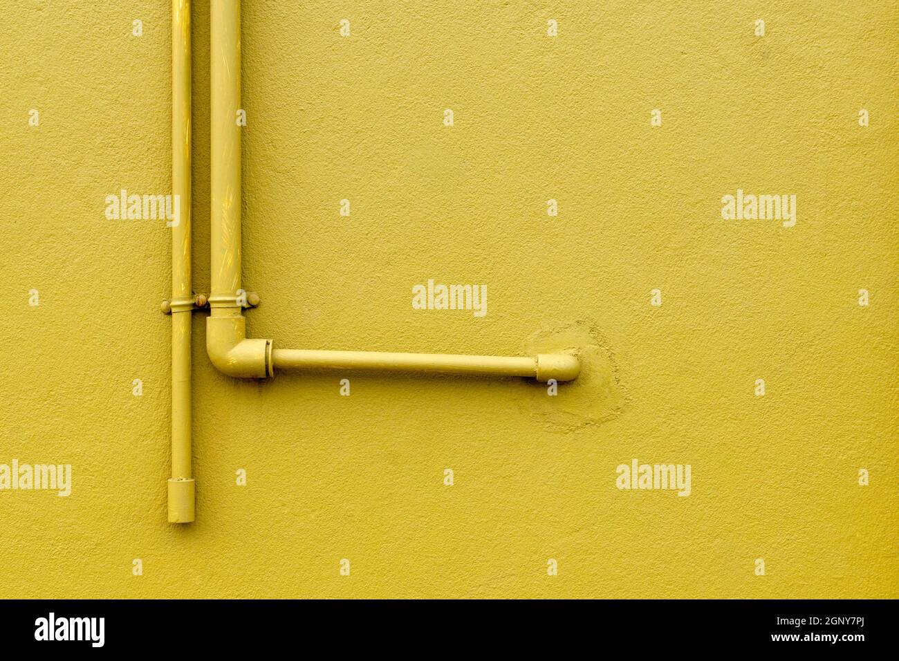 Plastic pipes connection in L shape attached on yellow colored concrete ...